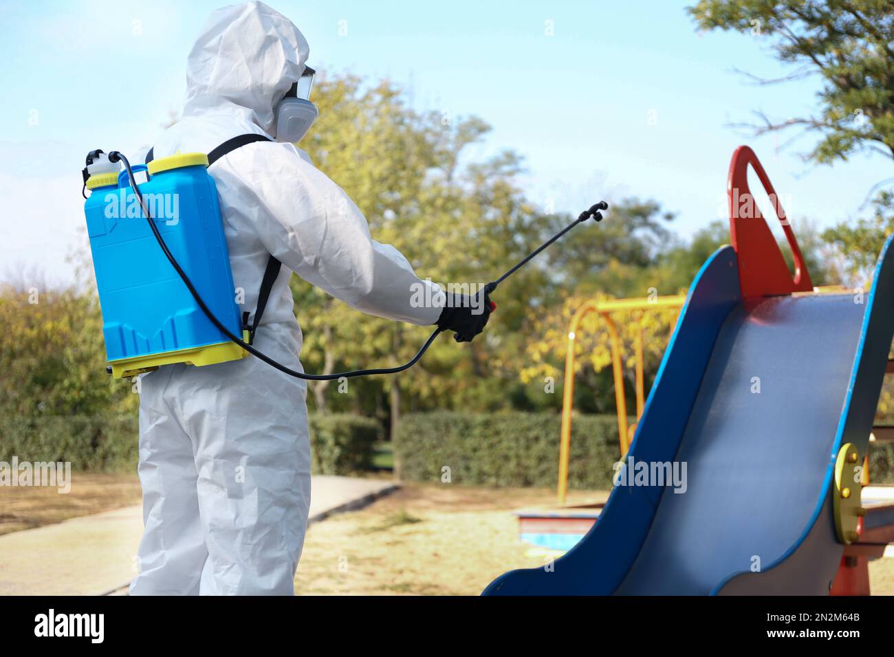 Person in hazmat suit with disinfectant sprayer near slide at children ...
