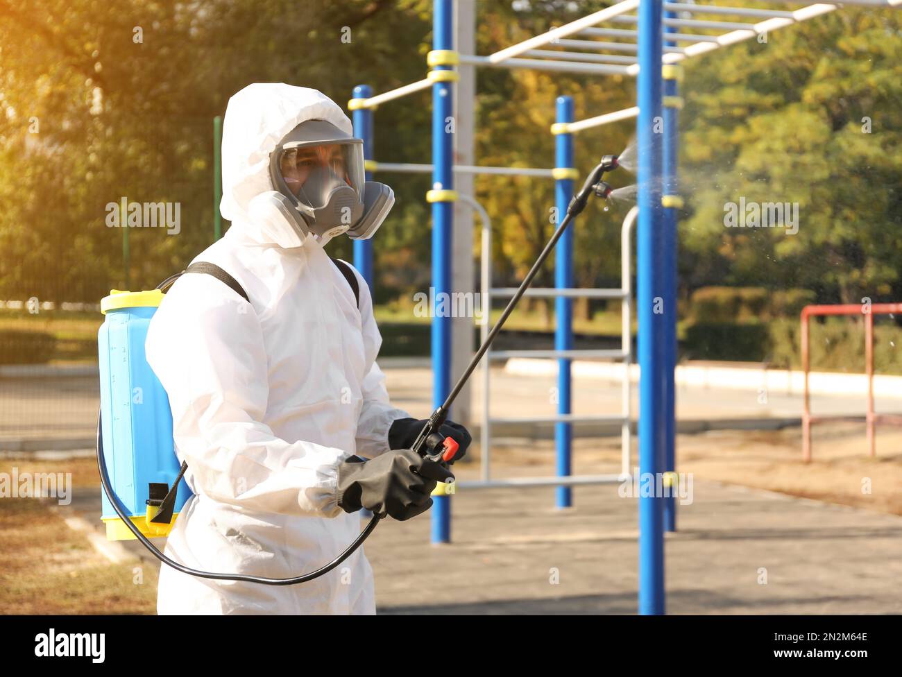Man in hazmat suit spraying disinfectant around outdoor gym. Surface ...