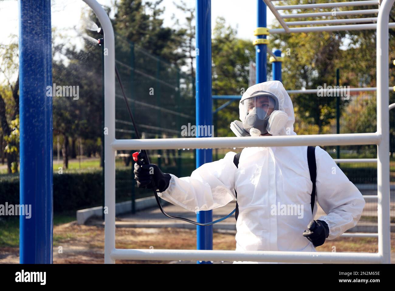 Man in hazmat suit spraying disinfectant on outdoor gym's equipment ...