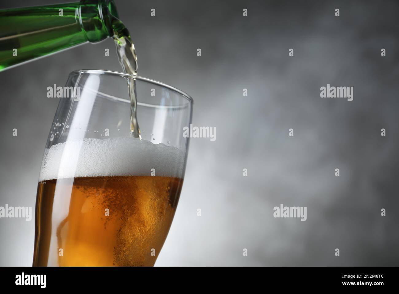 Pouring cold tasty beer from bottle into glass on grey background ...