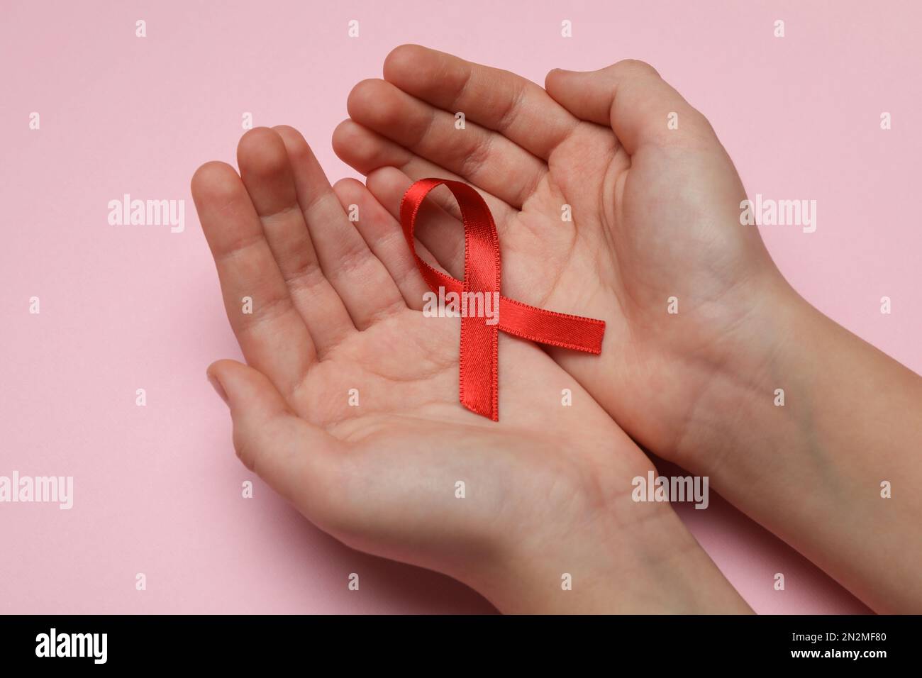 Little girl holding red ribbon on pink background, closeup. AIDS ...
