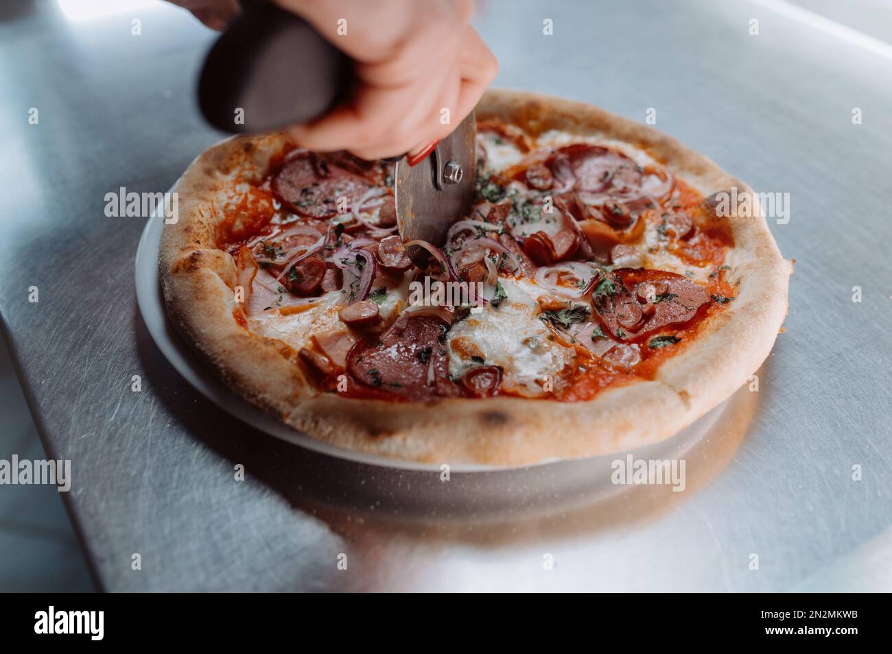 a man cuts a pizza into pieces. Closeup hand of chef baker in white ...