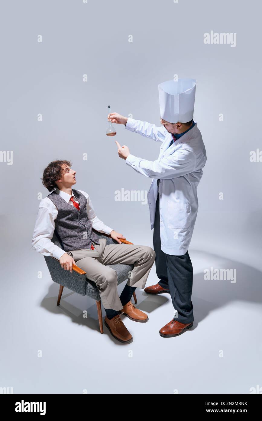 Doctor in white uniform showing to young man curing liquid over grey ...