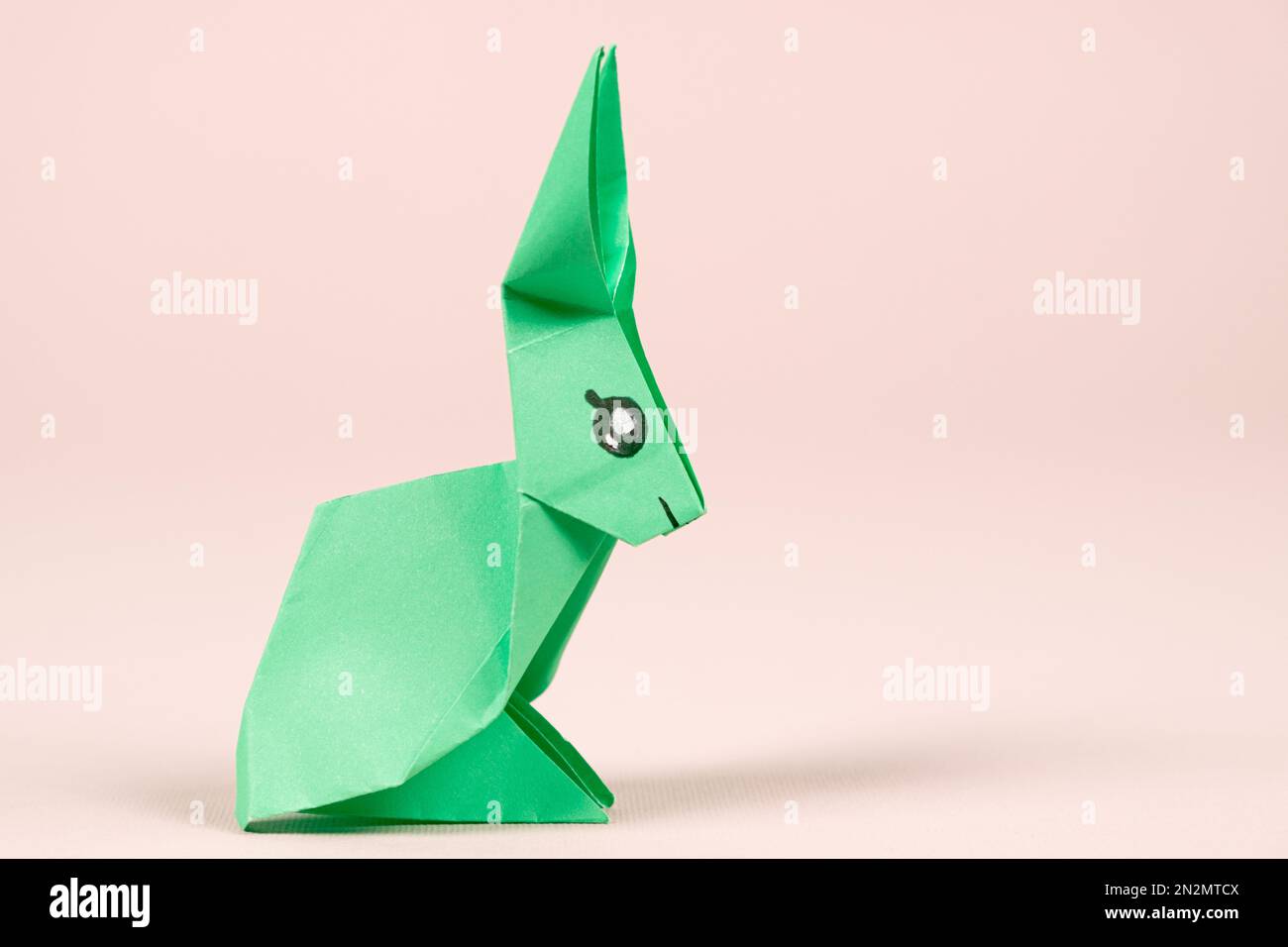A green origami rabbit on a beige background. Crafts for Easter, fold ...