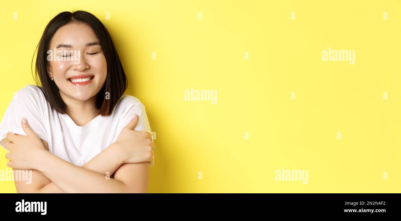 Close up of romantic asian girl hugging herself and dreaming, close ...