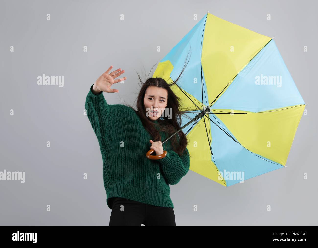 Emotional woman with umbrella caught in gust of wind on grey background ...