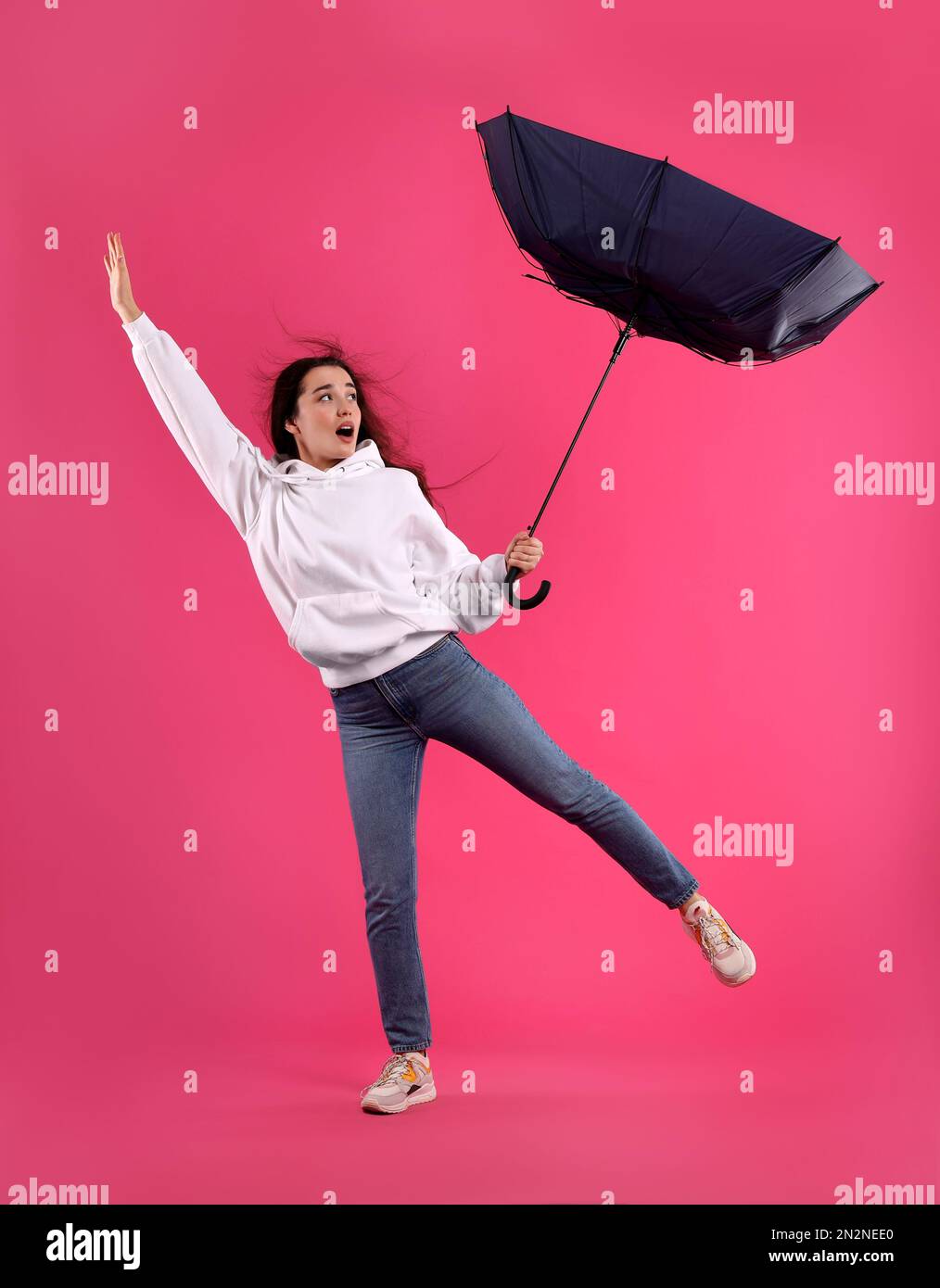 Emotional woman with umbrella caught in gust of wind on pink background ...