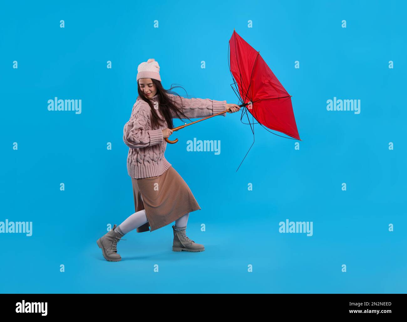 Young woman with umbrella caught in gust of wind on light blue ...