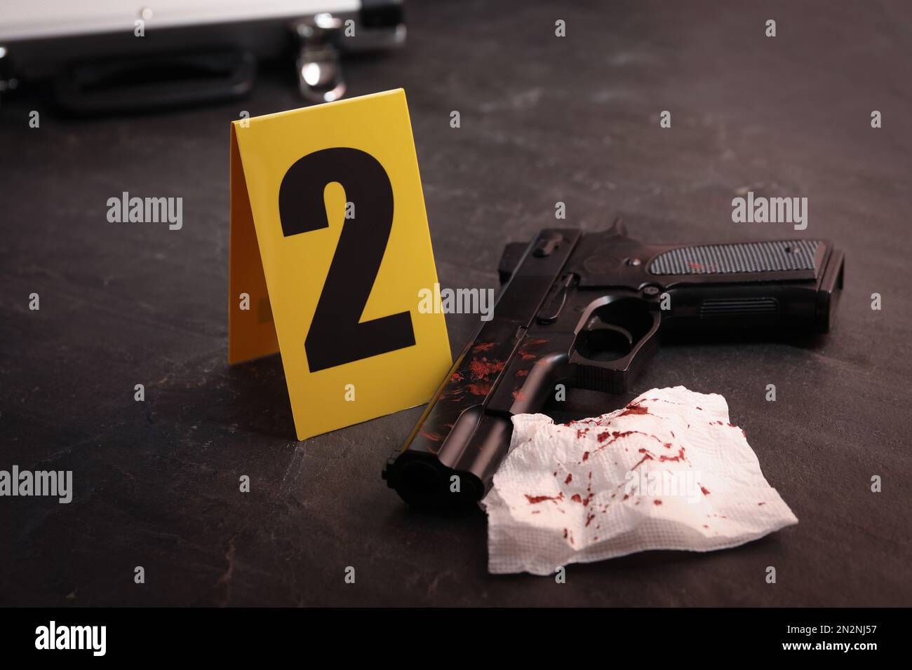 Napkin with blood, gun and evidence marker on black slate table ...