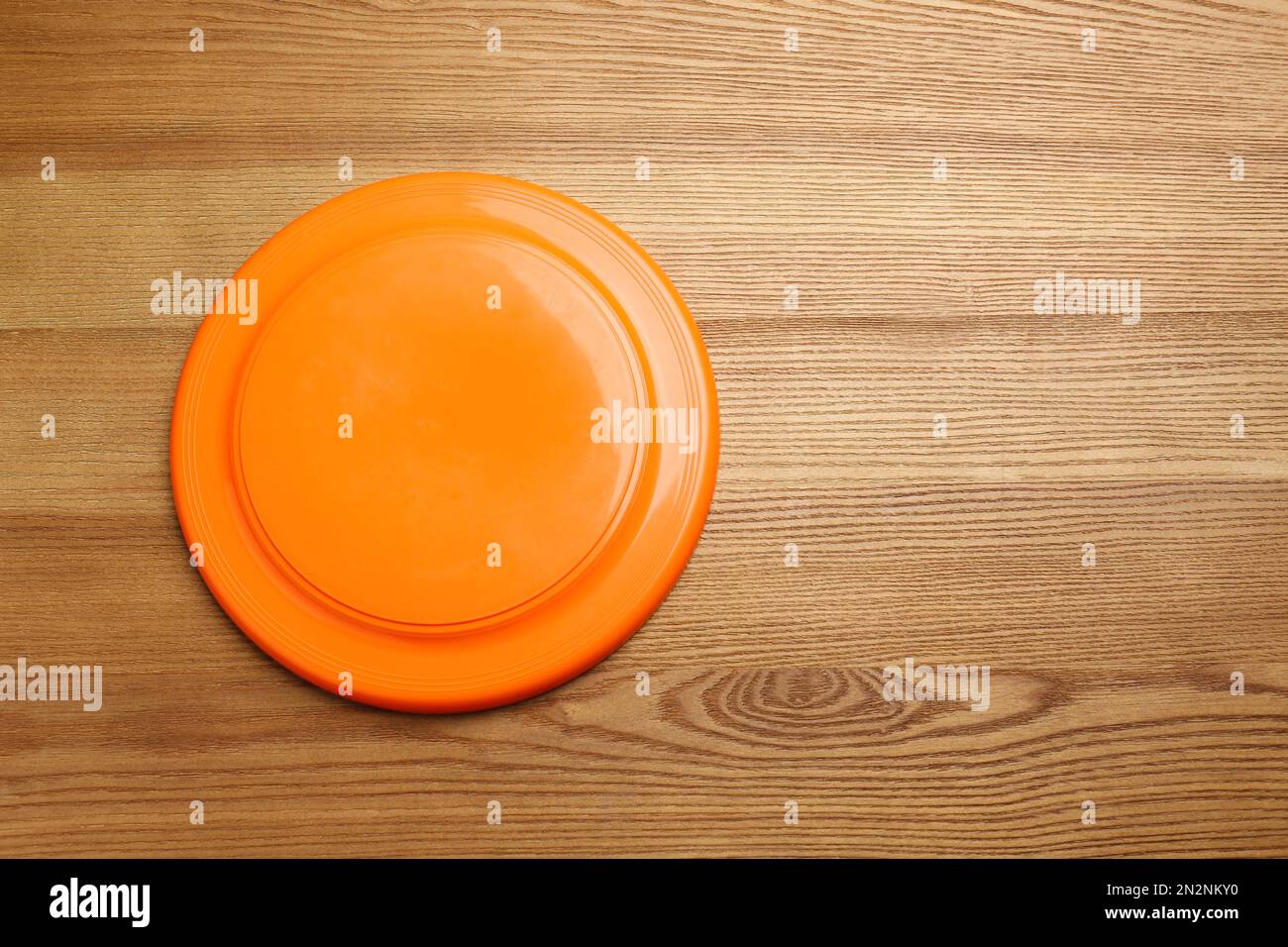 Orange plastic frisbee disk on wooden background, top view. Space for ...