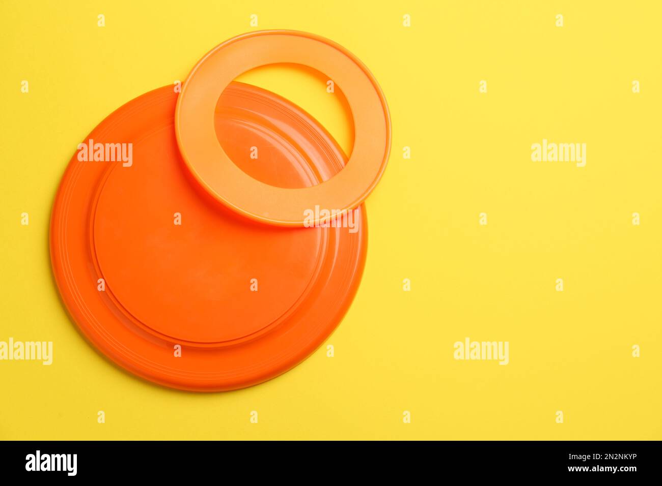 Plastic frisbee disk and ring on yellow background, flat lay. Space for ...