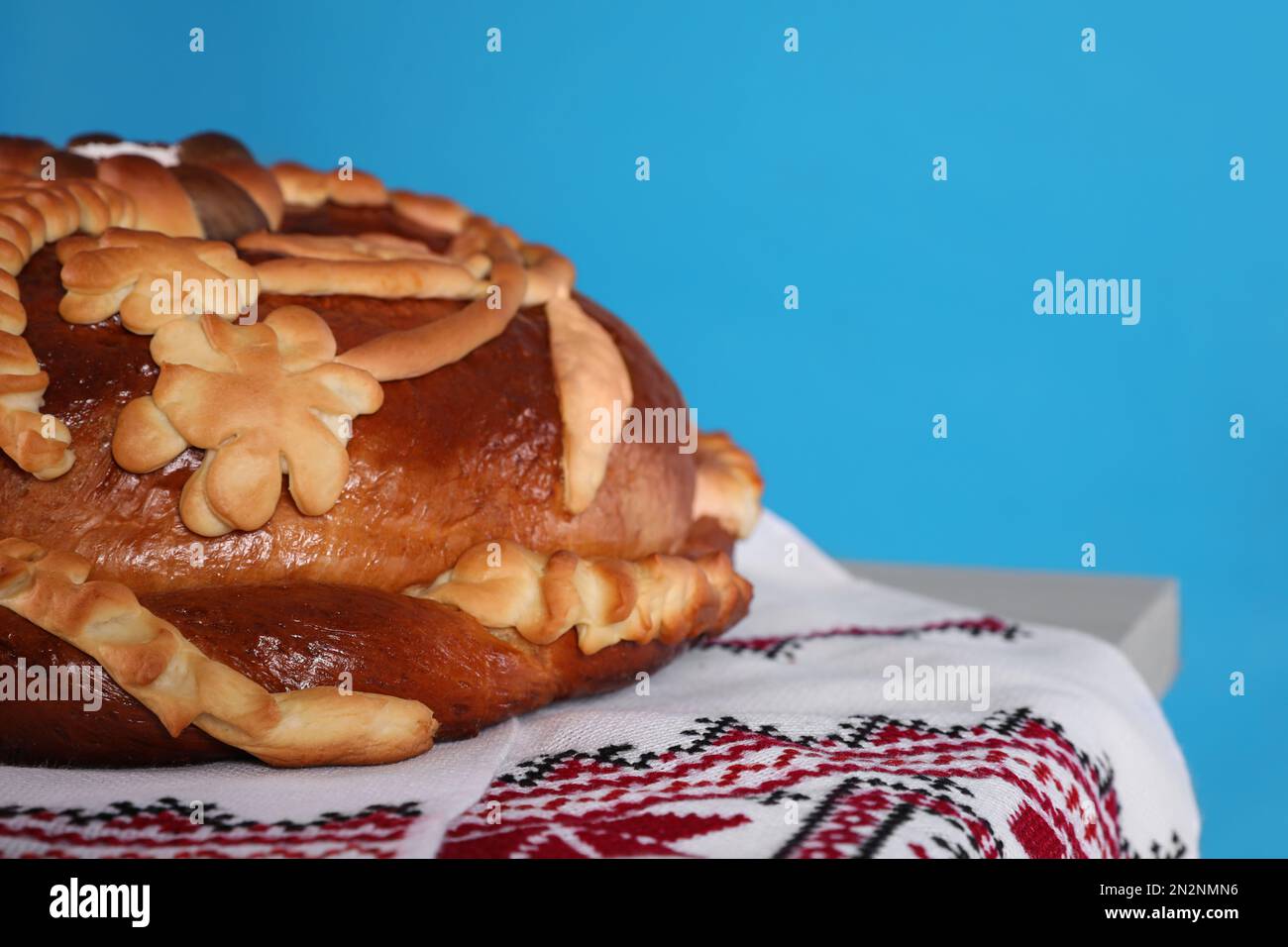 Rushnyk with korovai on light blue background, closeup. Ukrainian bread ...