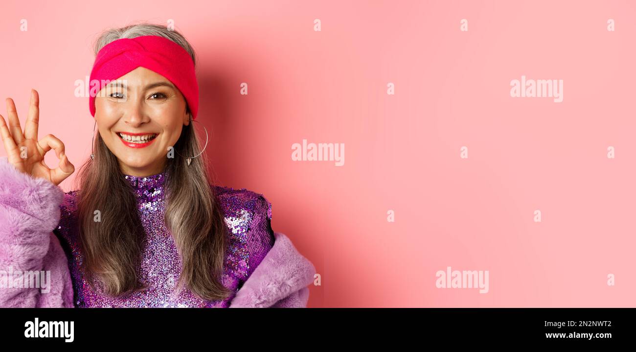 Fashion. Close-up of asian old lady in stylish disco outfit showing OK ...