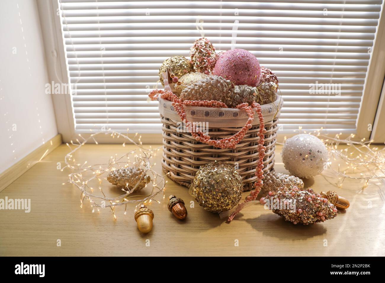 Basket with beautiful Christmas tree baubles and fairy lights on window ...