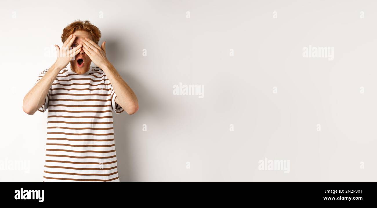 Shocked and embarrassed redhead guy covering eyes, peeking through ...