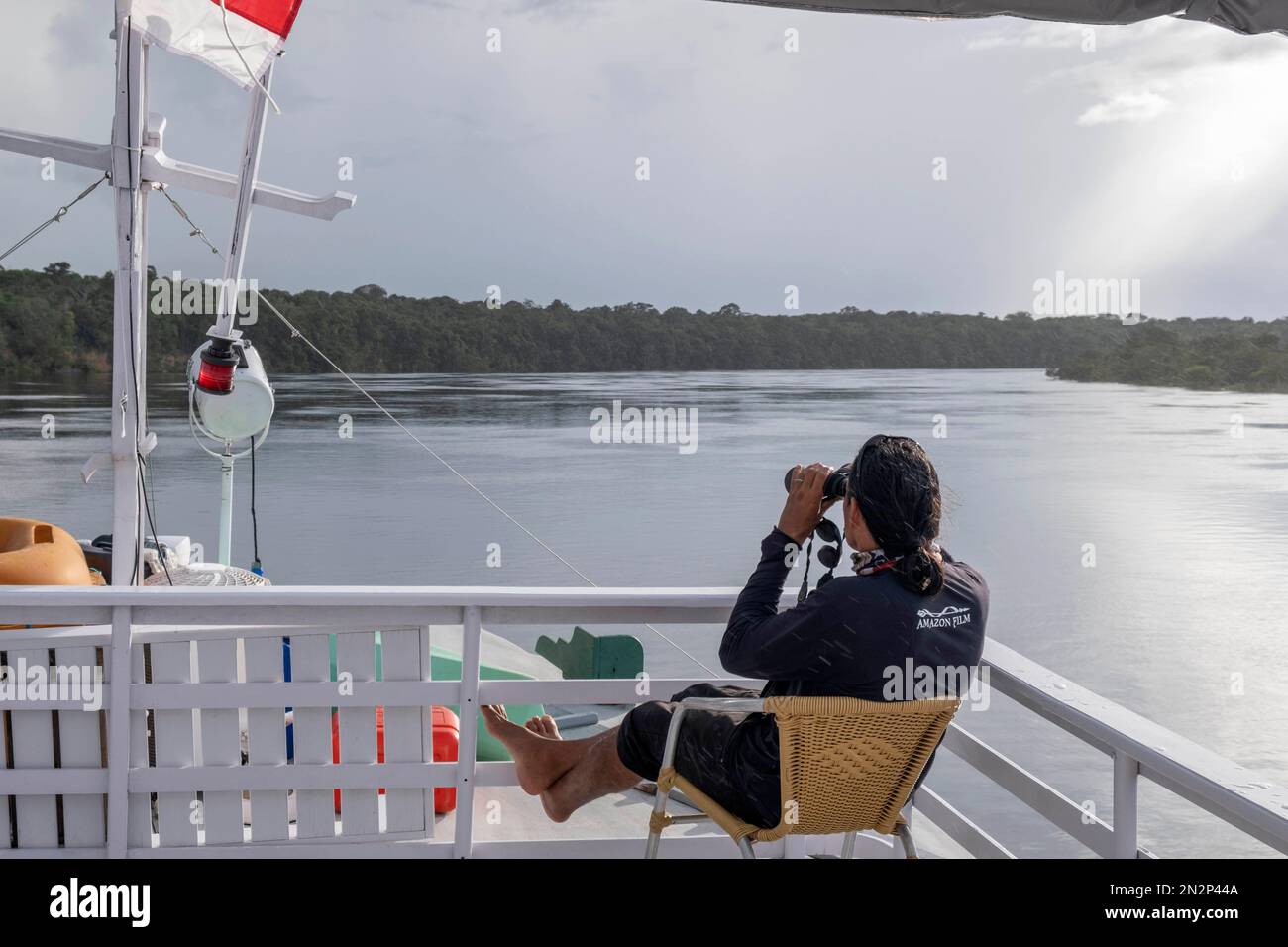A jungle guide looking at the forest with binoculars from the deck of ...