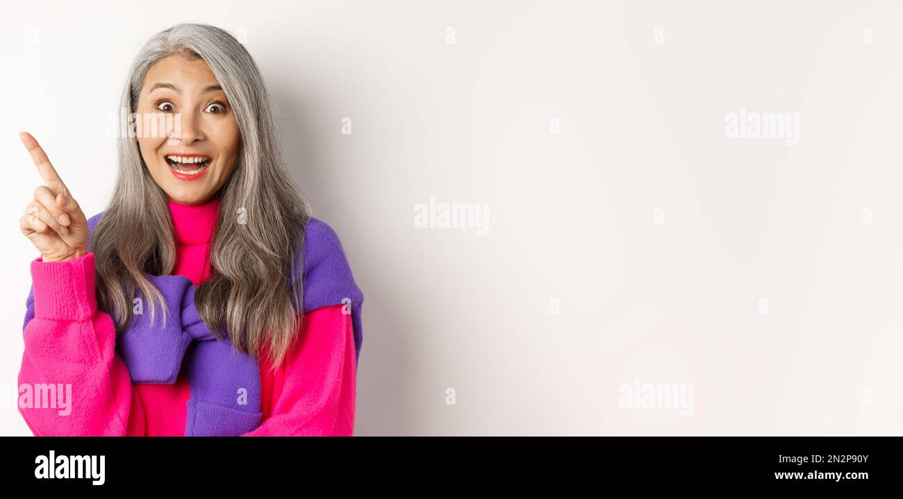 Close up of beautiful asian female model pointing finger at upper left ...