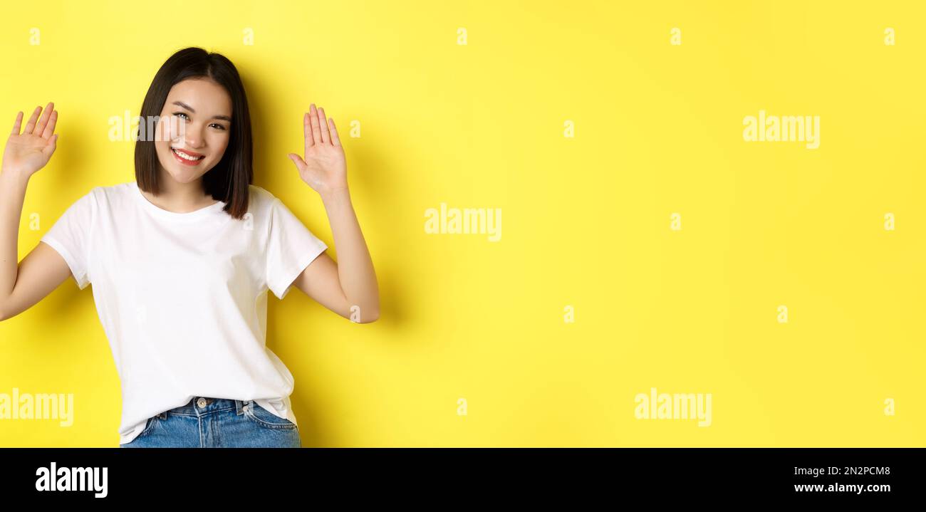 Friendly young asian woman saying hello, raising empty hands up and ...
