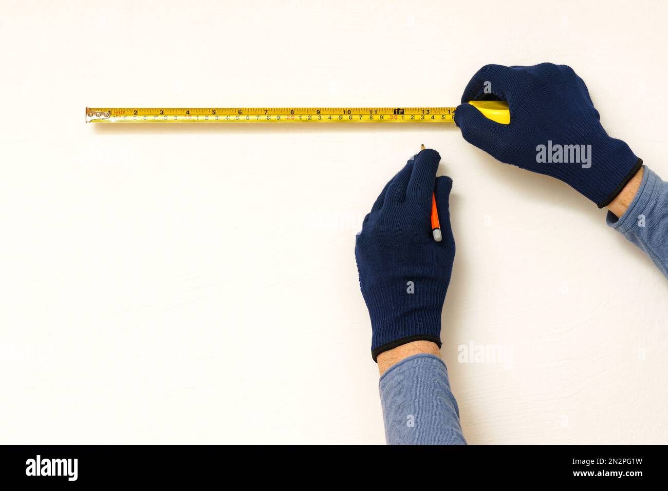 Builder's hands with measuring tape and pencil on white wall. Close up ...