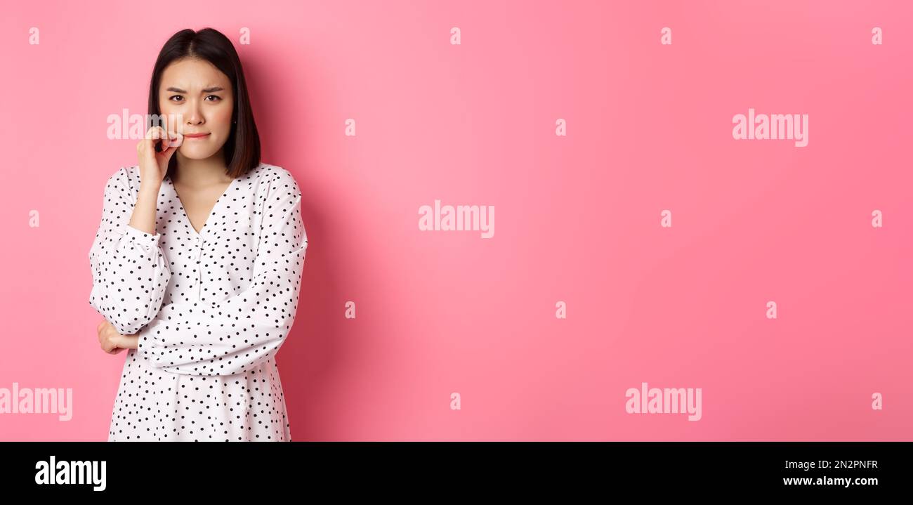Brunette asian woman in dress looking displeased, frowning and zipping ...
