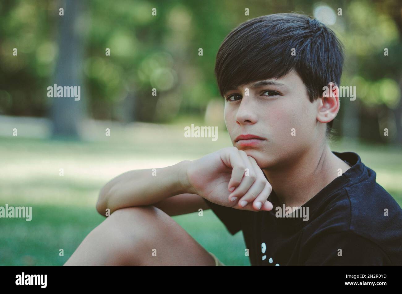 Portrait of a teenage boy sitting in Parque del Retiro in summer ...
