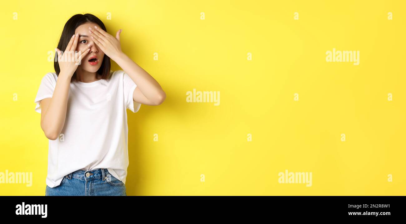 Intrigued asian girl waiting for surprise, peeking through fingers on ...