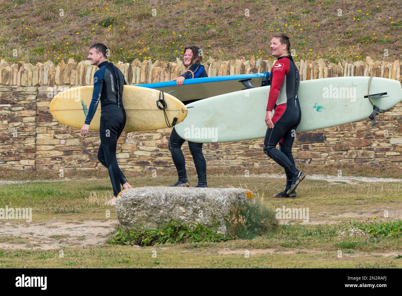 Three surfers carrying their surfboards and walking on the coast path ...