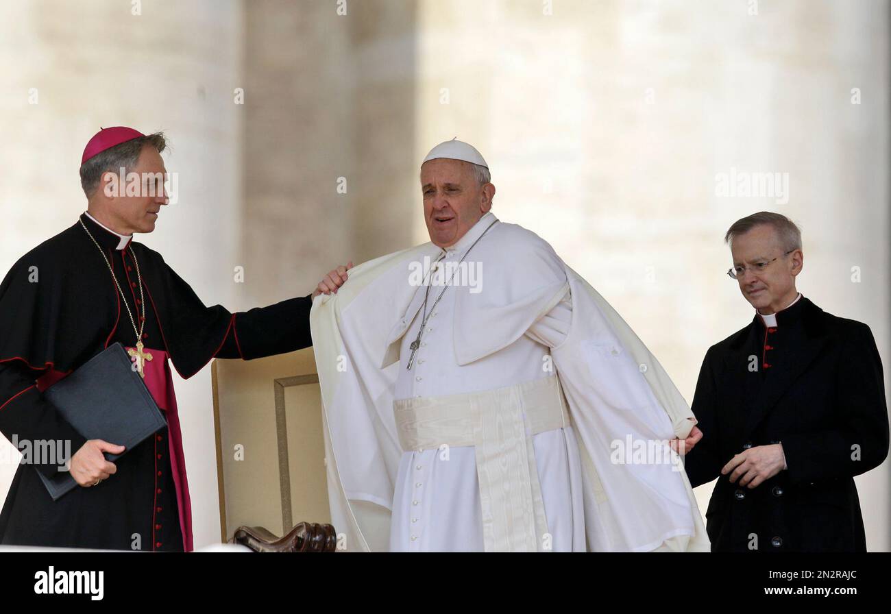 Pope Francis helped by Monsignor Georg Gaenswein, takes off his coat ...
