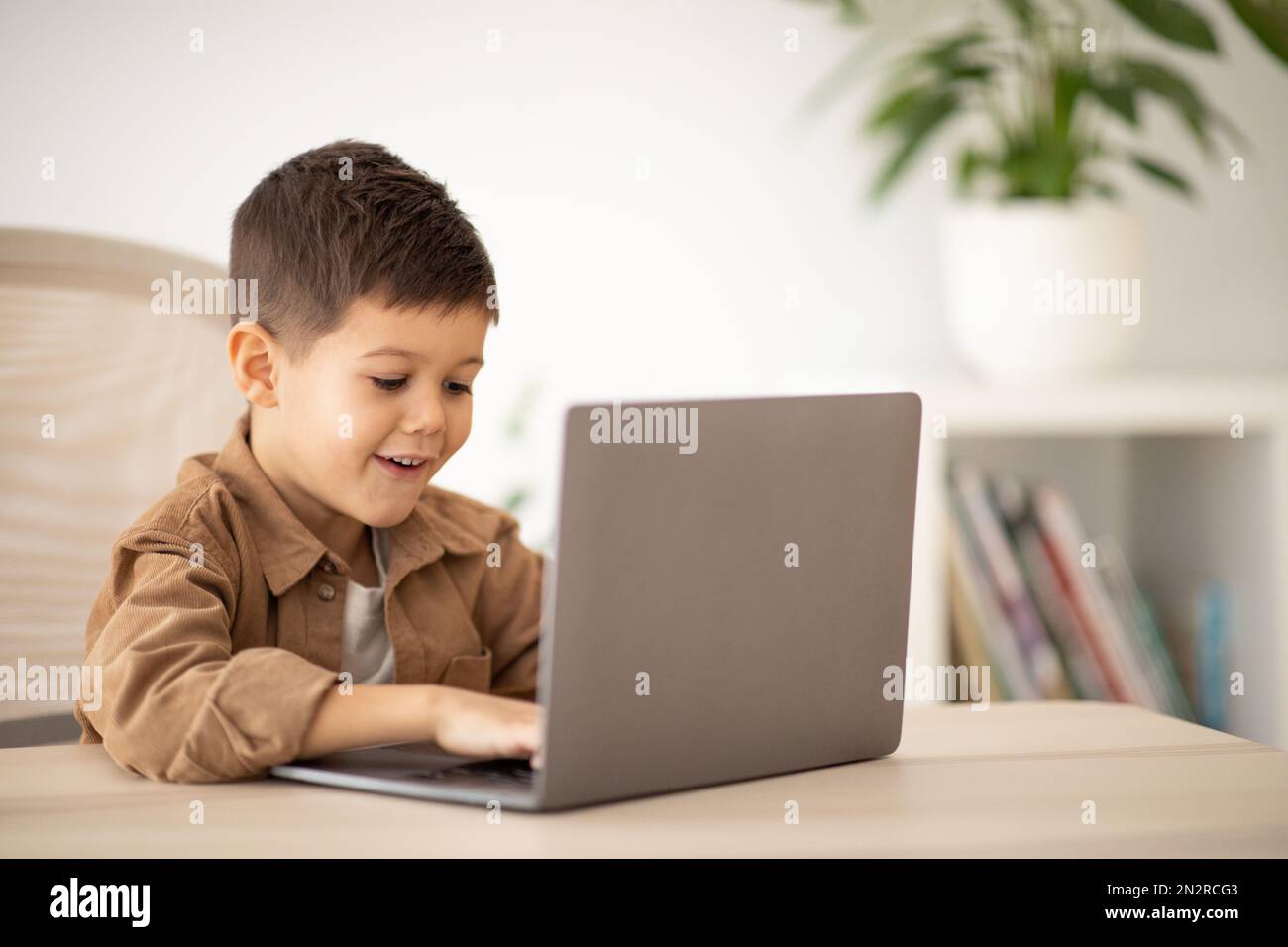 Glad surprised cute caucasian little child pupil sits at table, typing ...