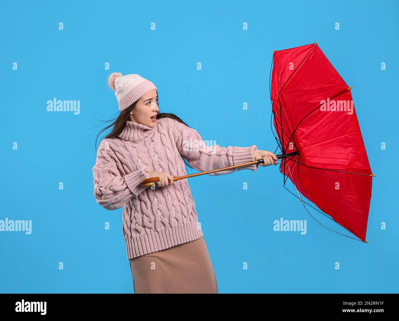 Young woman with umbrella caught in gust of wind on light blue ...