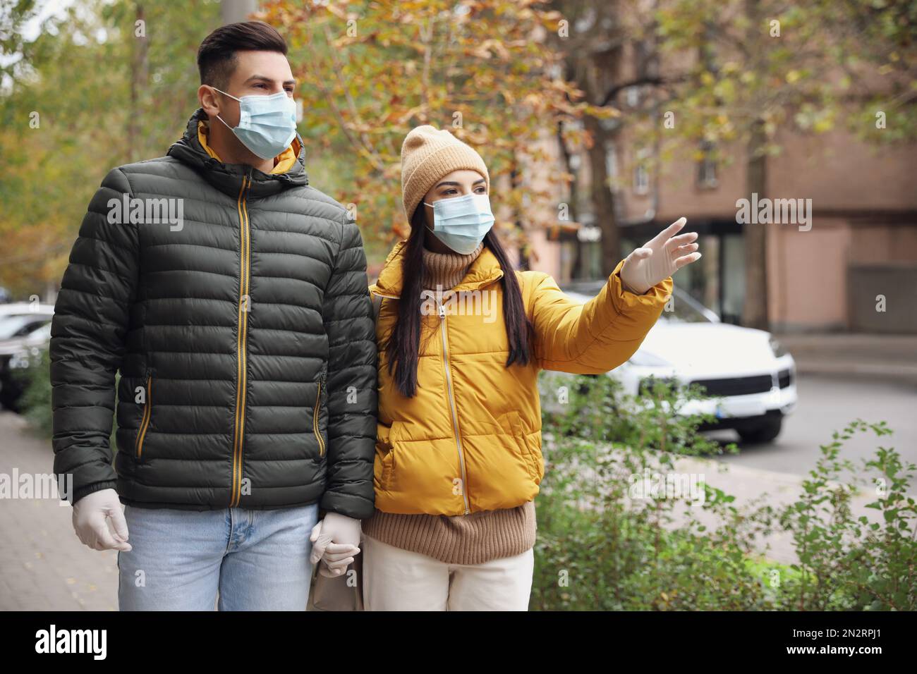 Couple in medical face masks and gloves walking outdoors. Personal ...
