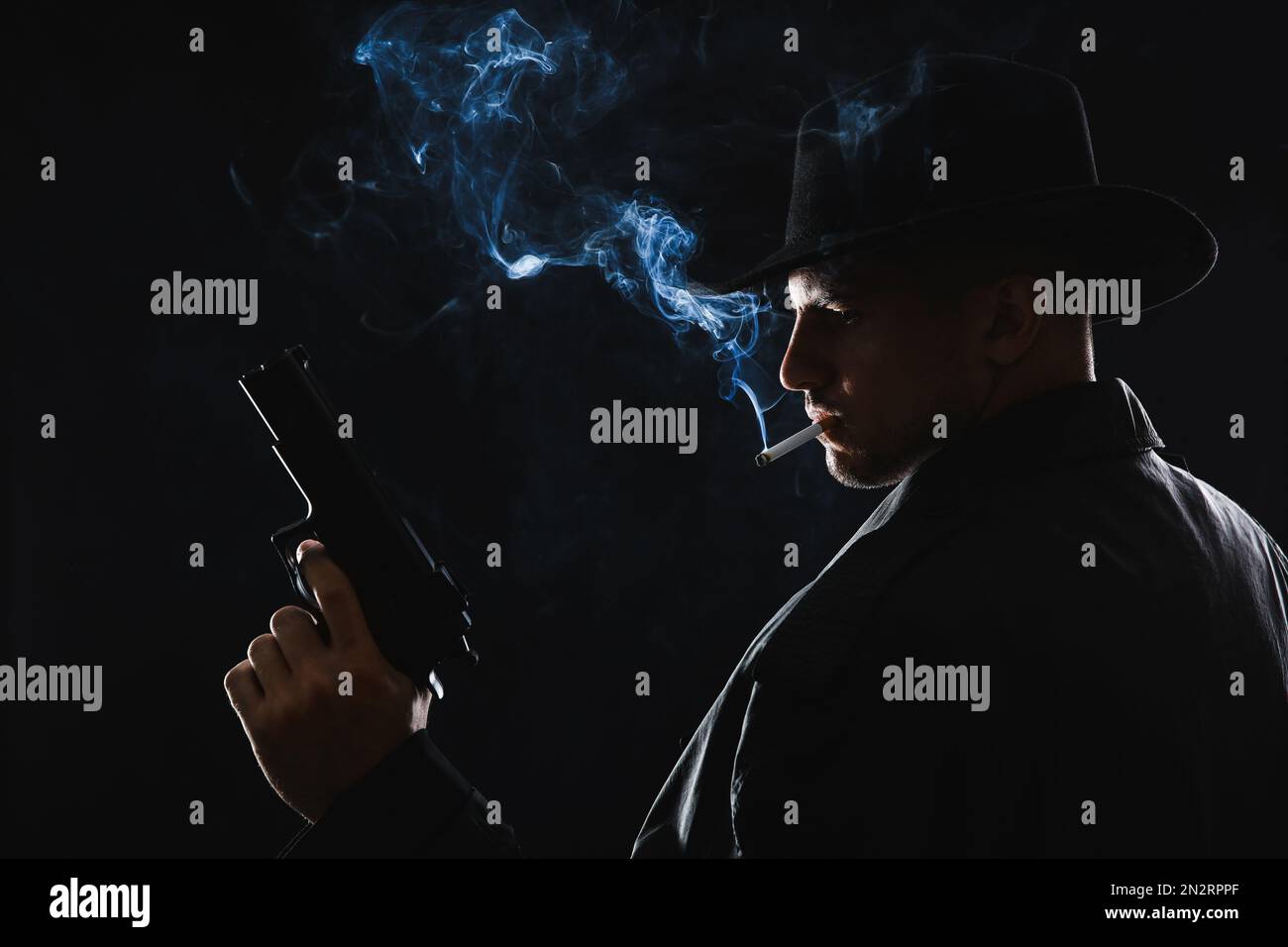 Old fashioned detective with gun smoking cigarette on dark background ...