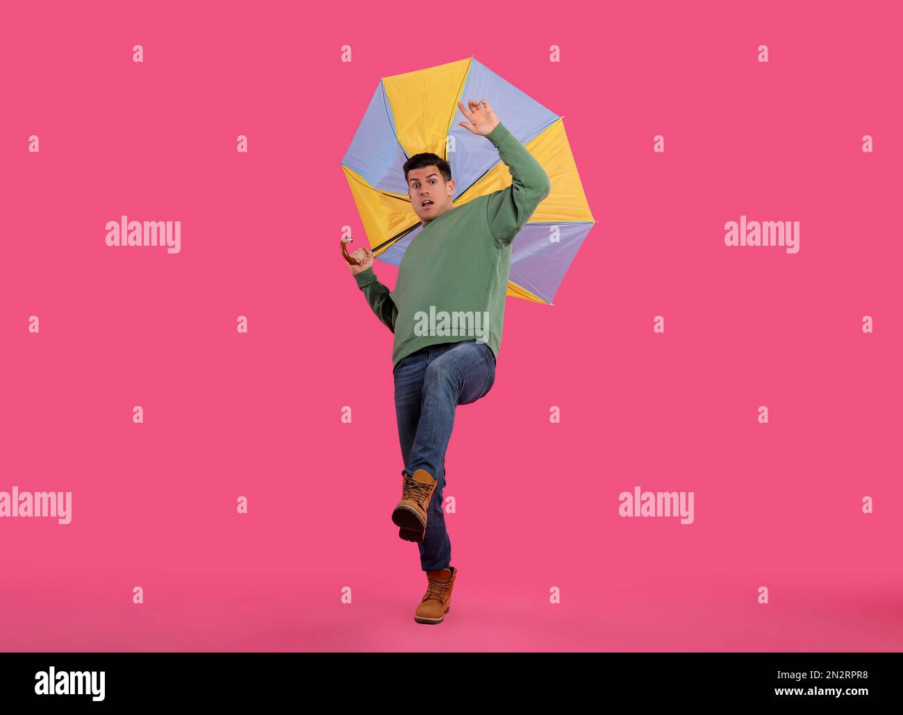 Emotional man with umbrella caught in gust of wind on pink background ...