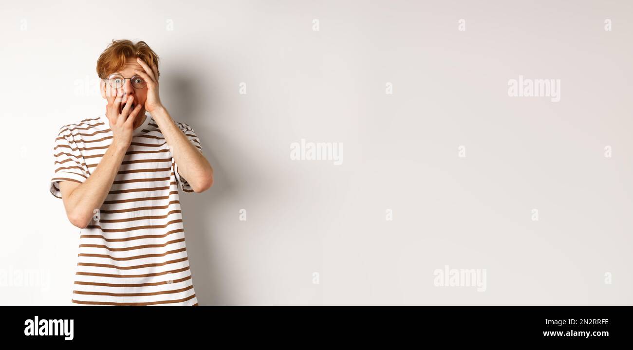 Scared redhead guy screaming terrified, holding hands on face from fear ...