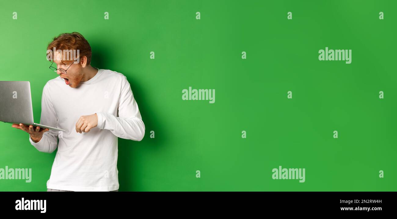 Image of young redhead man looking surprised at laptop screen, drop jaw ...