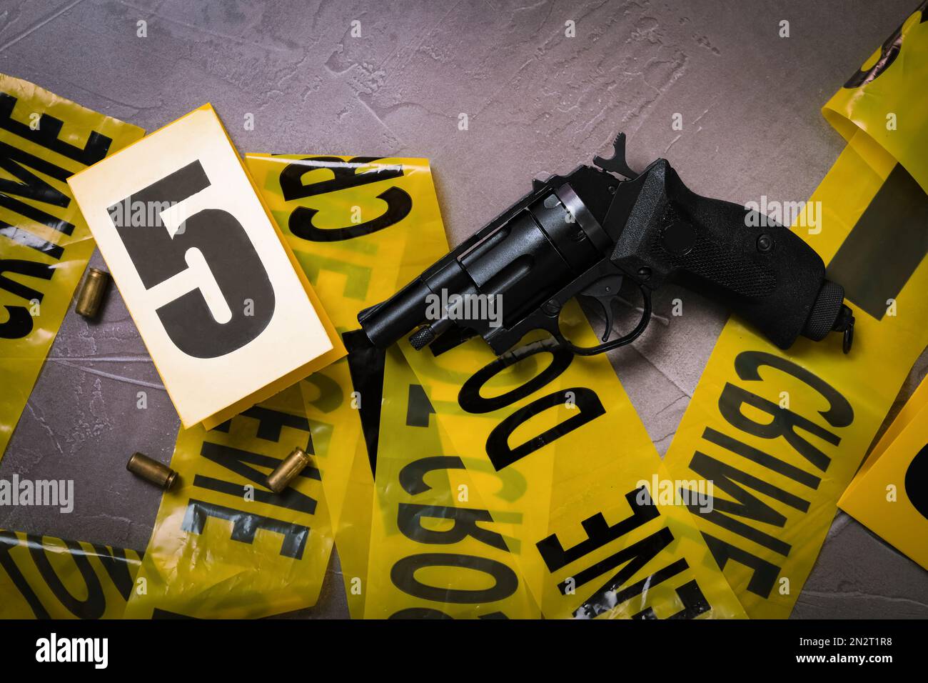 Flat lay with yellow tape, crime scene marker and gun on grey stone ...