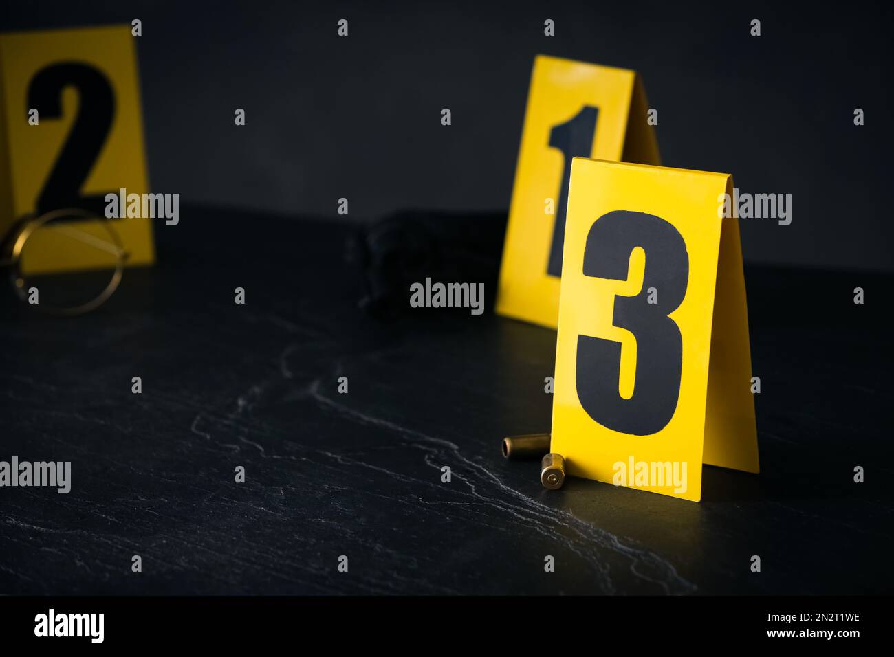 Shell casings and evidence marker on black slate table, closeup. Crime ...