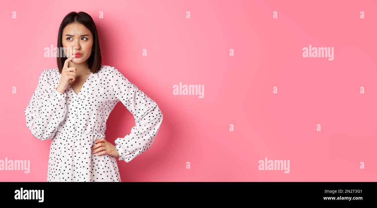 Troubled asian girl making decision, frowning and touching lip while ...