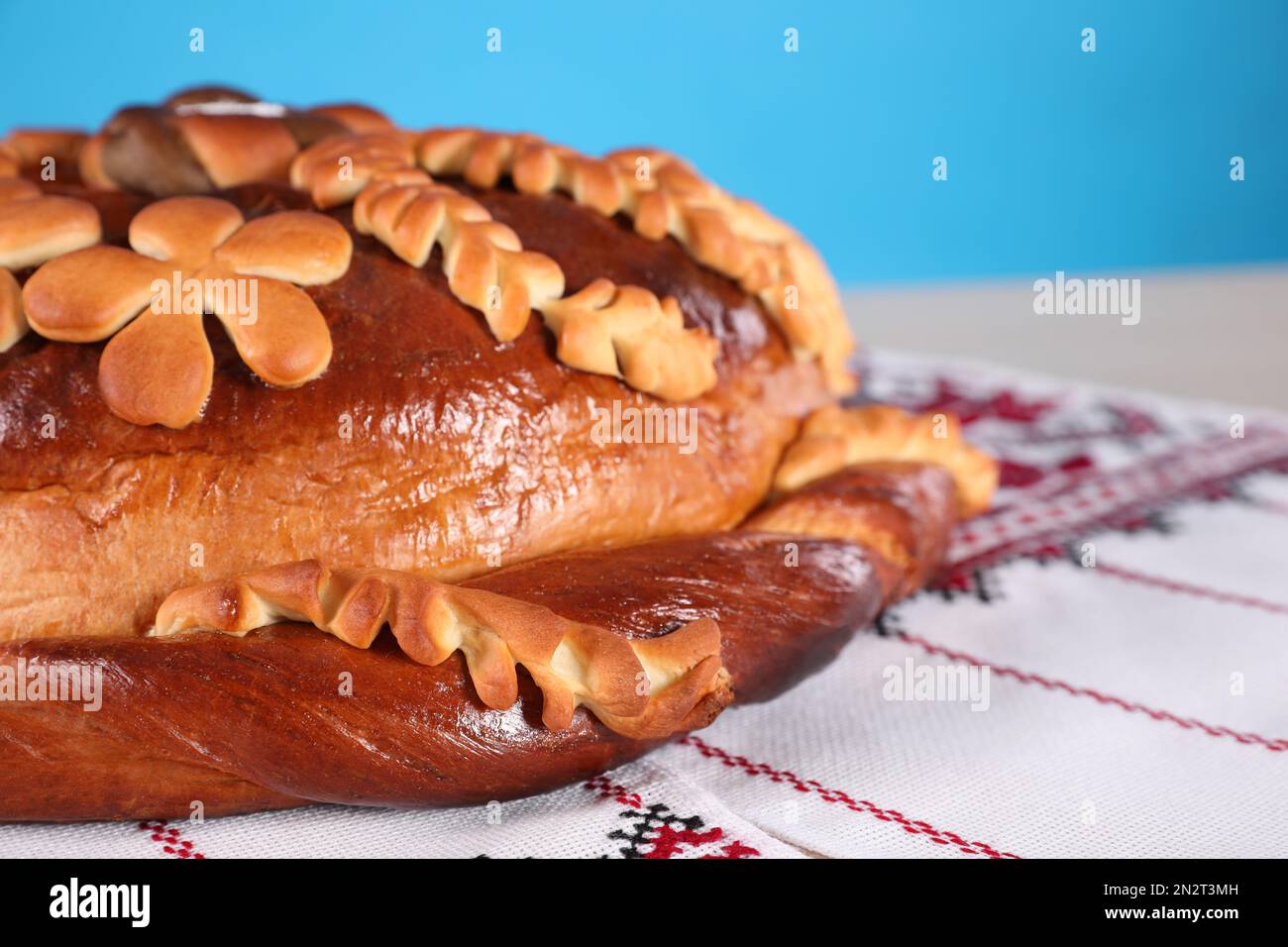 Rushnyk with korovai on light blue background, closeup. Ukrainian bread ...