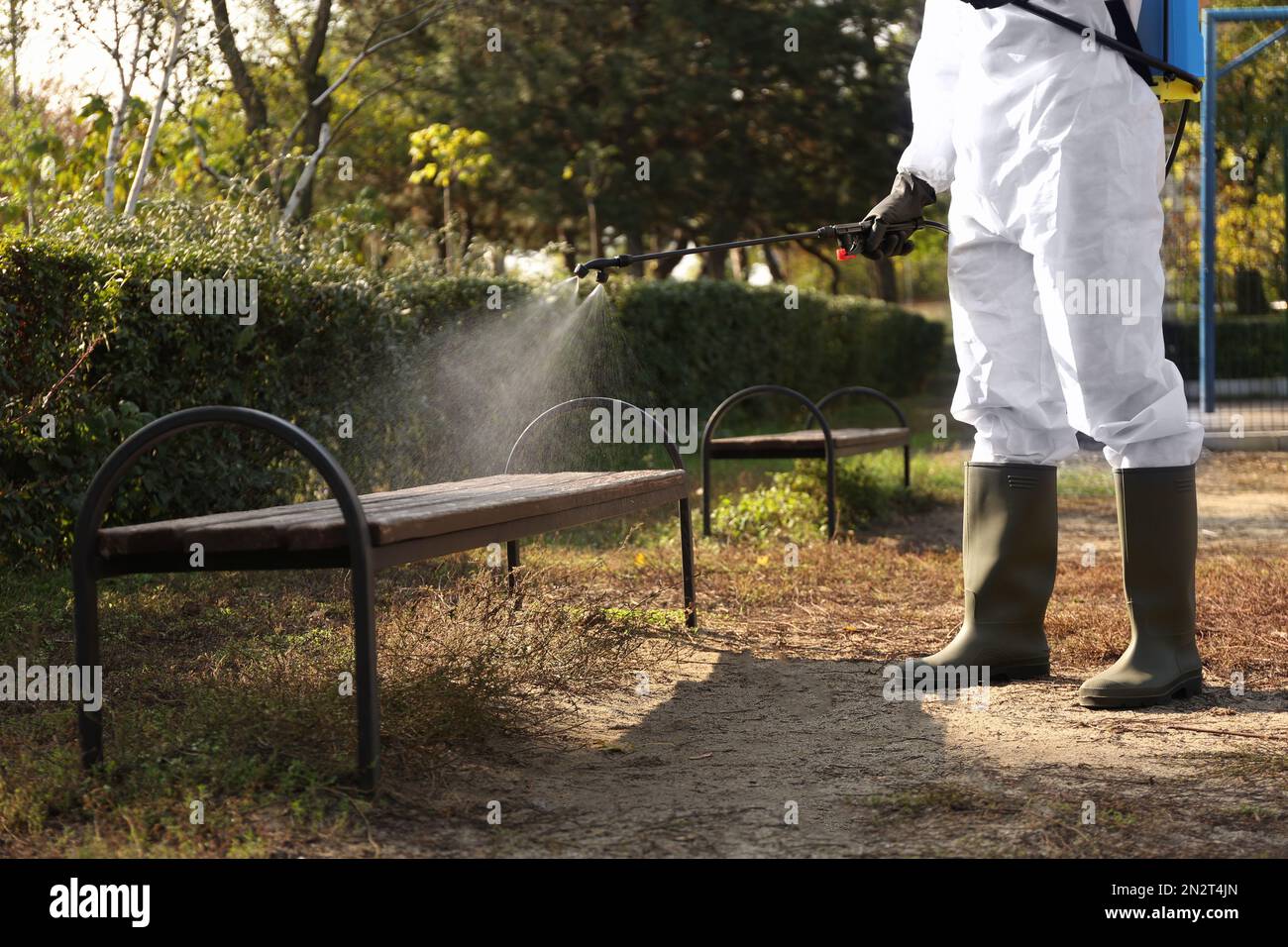 Person in hazmat suit spraying disinfectant onto bench outdoors ...