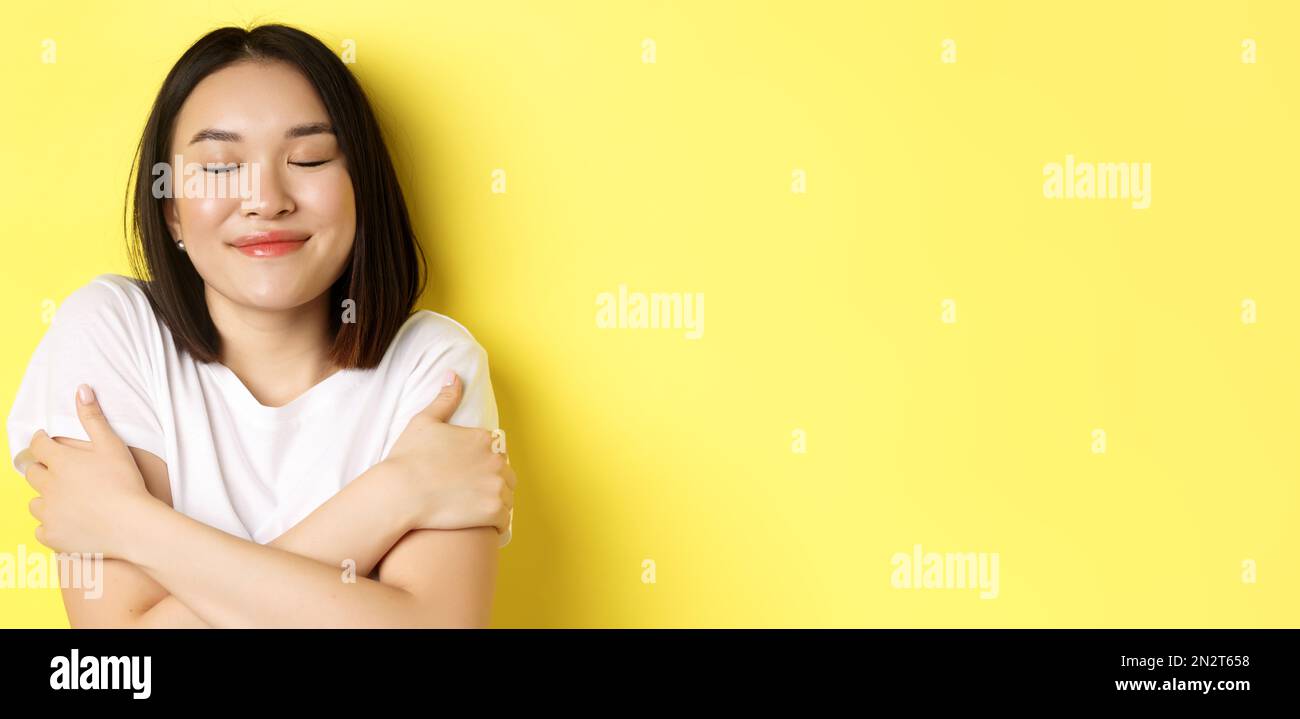 Close up of romantic asian girl hugging herself and dreaming, close ...