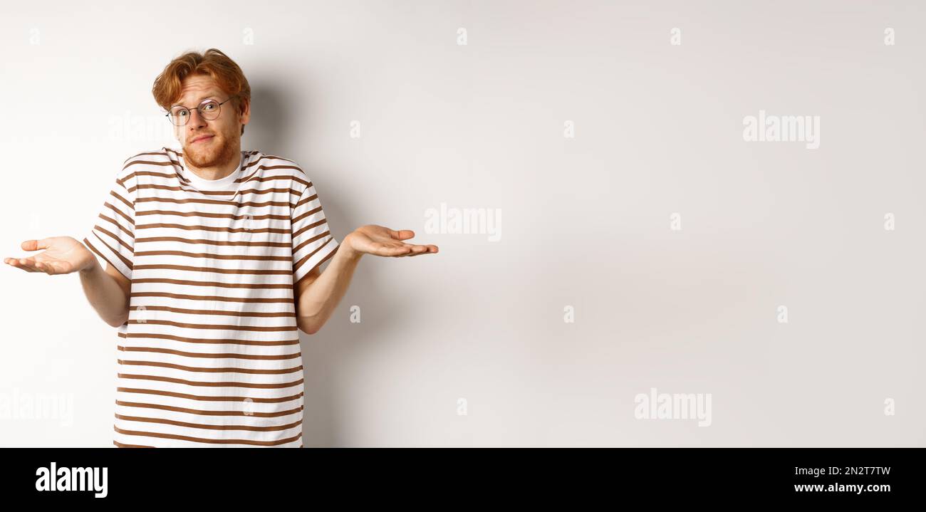 Confused young man with red hair, shrugging shoulders and looking ...