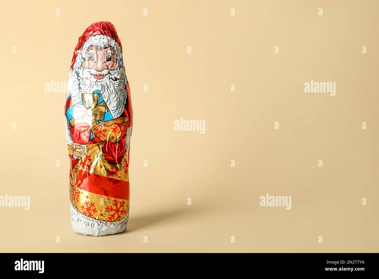 Chocolate Santa Claus in foil wrapper on beige background. Space for ...