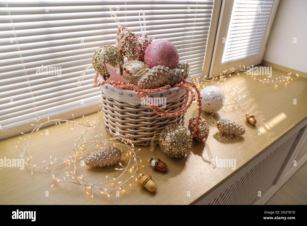 Basket with beautiful Christmas tree baubles and fairy lights on window ...