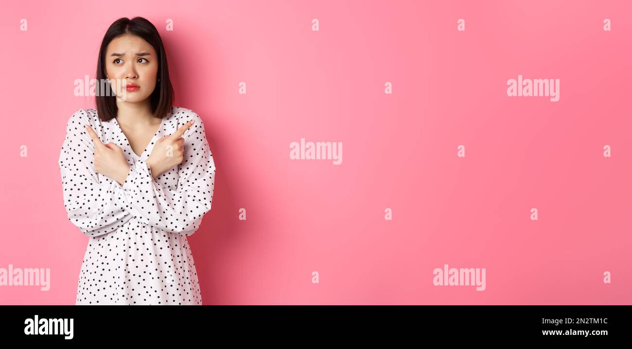 Concerned asian woman having doubts, pointing sideways and looking left ...
