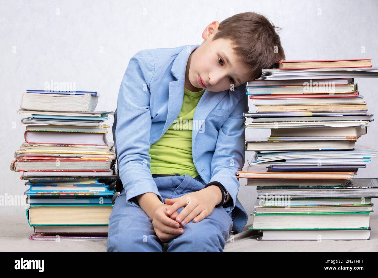 A tired school-age boy sits between stacks of books. Sad child with ...