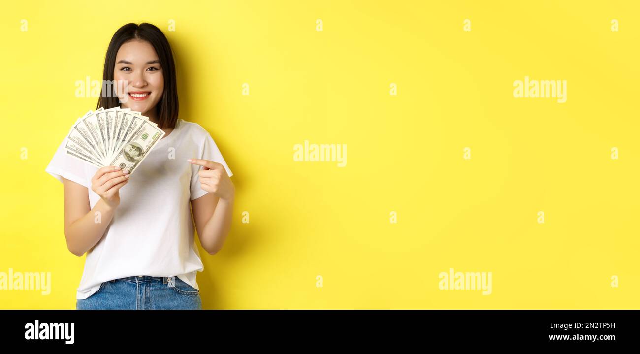 Young asian woman smiling, showing prize money, pointing finger at ...