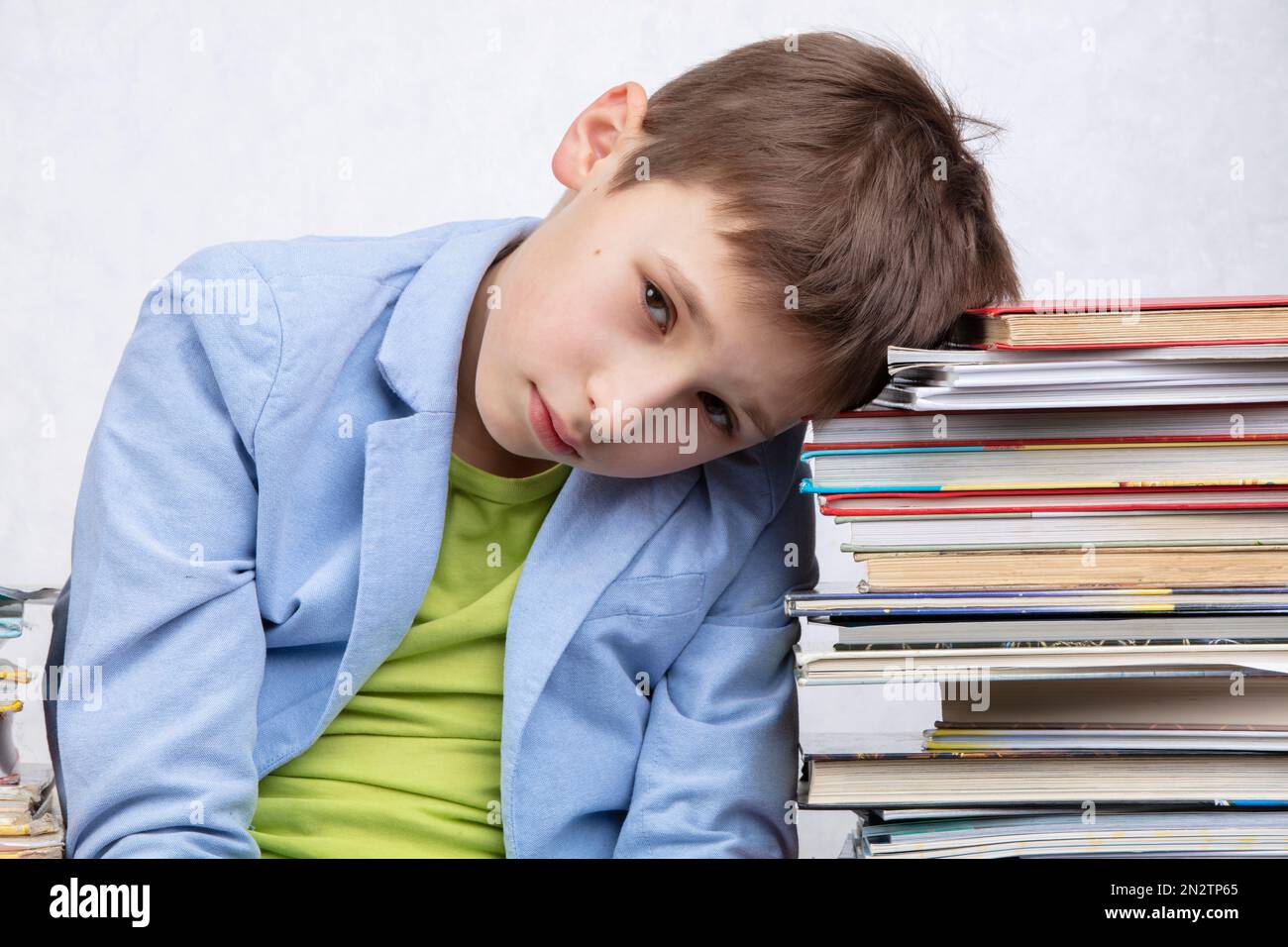 A tired school-age boy sits between stacks of books. Sad child with ...