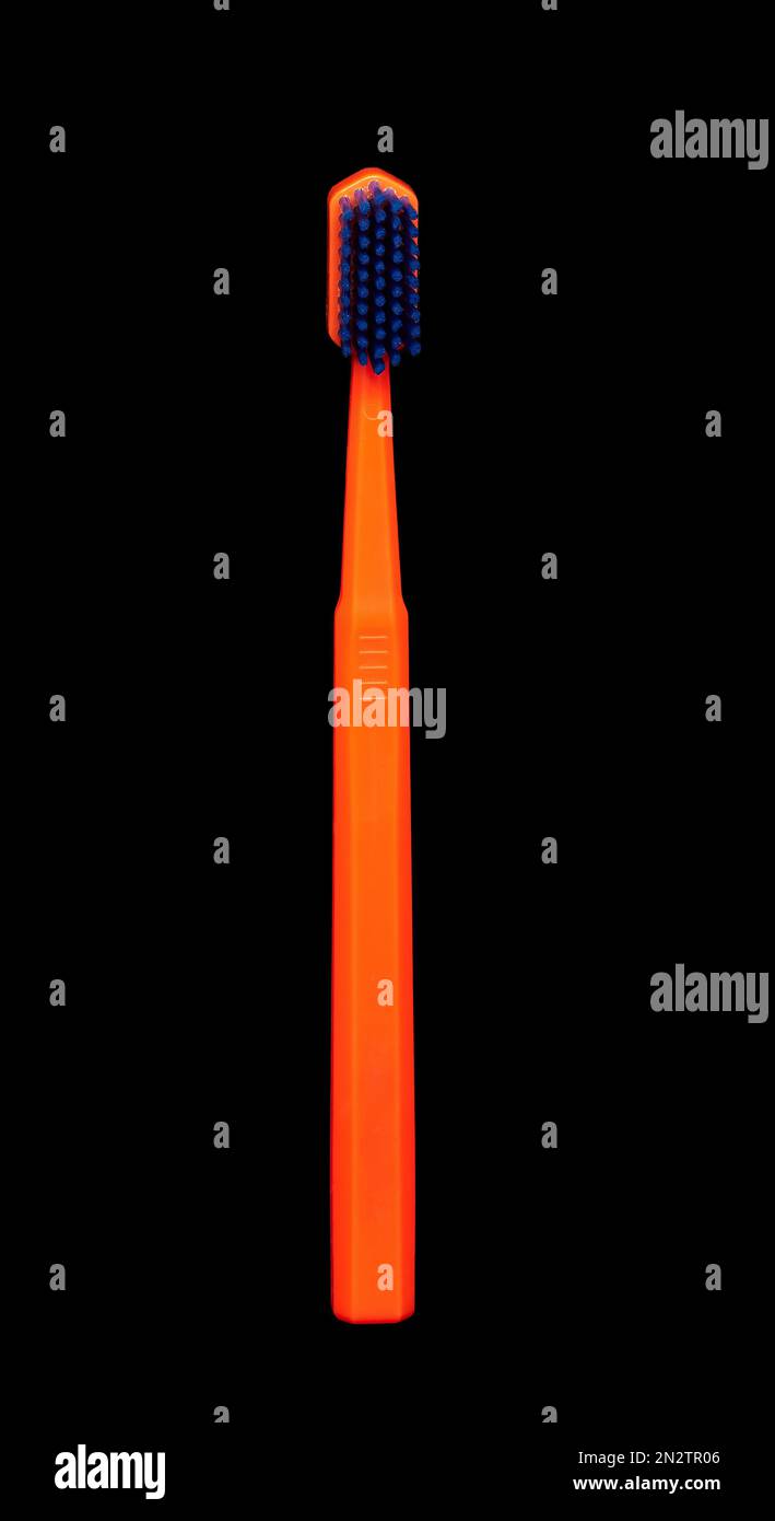 Image of an orange toothbrush with blue bristles on a black background ...