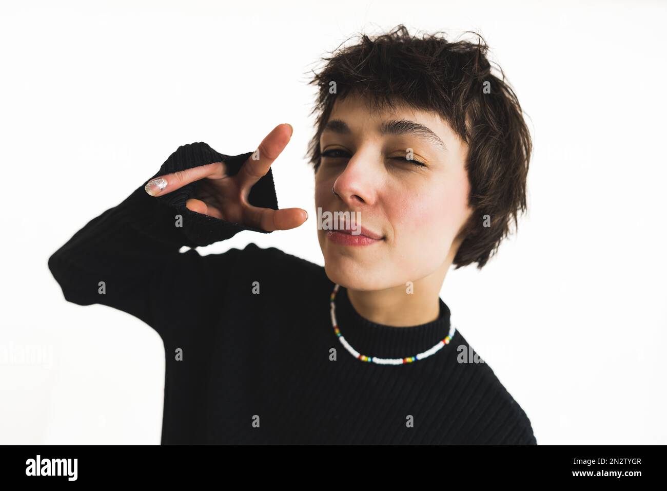 Cool short-haired Gen Z woman blinking at camera and showing v sign ...
